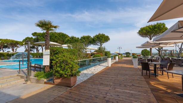 Um deck de madeira com área de estar externa, piscina e vegetação.