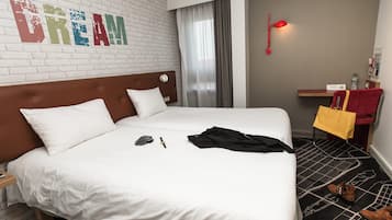 Quarto de hotel com parede de tijolos brancos, cabeceira marrom, edredom branco, luminária vermelha, cadeira vermelha e tapete com padrão preto e branco.
