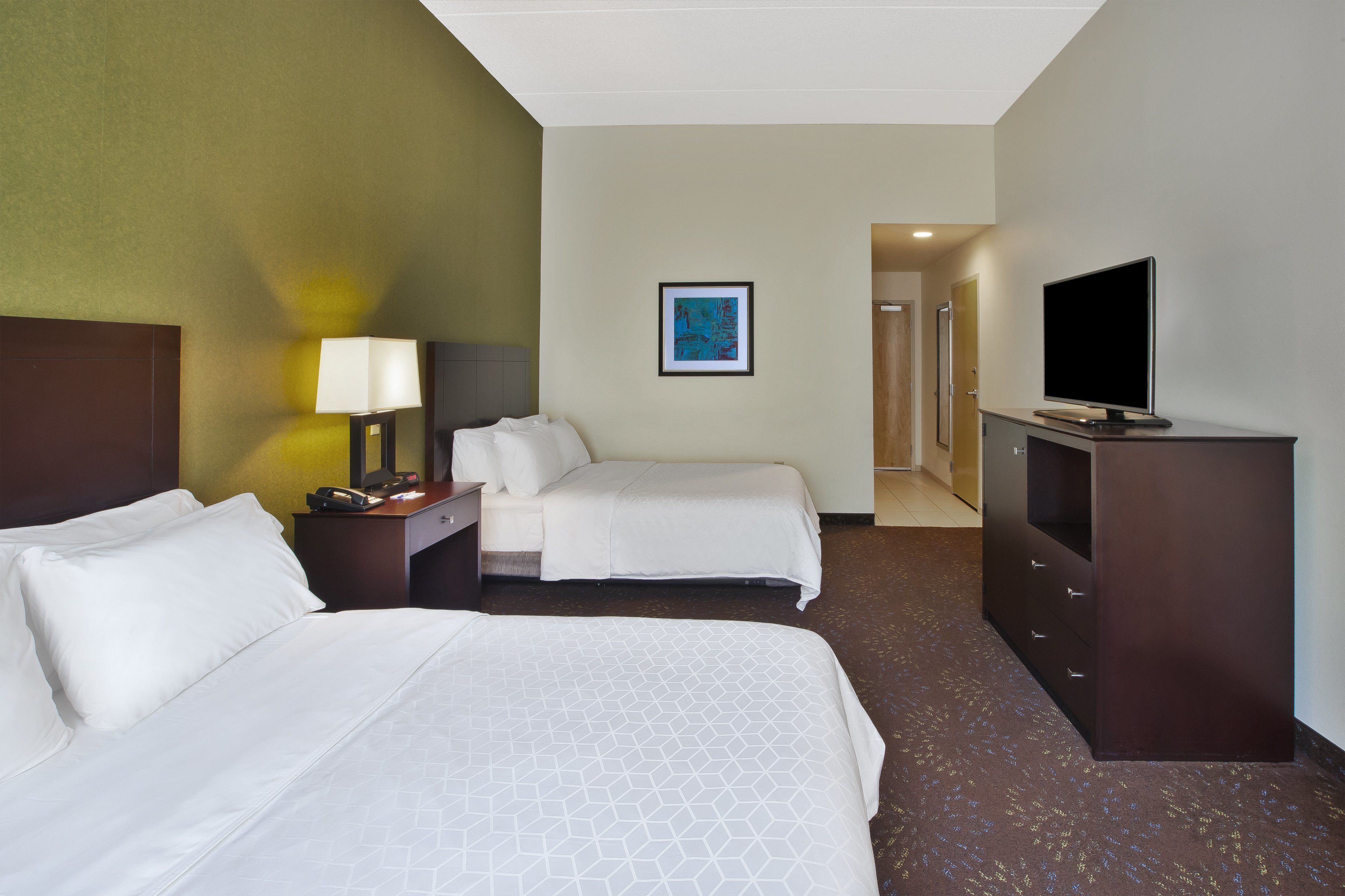 Quarto de hotel com duas camas, uma escrivaninha com abajur, uma televisão num armário e um quadro na parede.