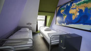 Quarto com duas beliches de metal, uma parede de destaque verde, um grande mapa-múndi e um pequeno armário preto.