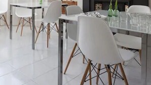 Uma sala de jantar moderna com uma mesa de vidro, cadeiras brancas, um ventilador de teto e uma lareira.