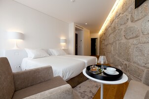 Quarto de hotel com duas camas, um sofá, uma pequena mesa com uma bandeja de itens de café da manhã e uma parede de pedra.