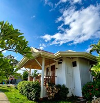 Uma casa térrea com varanda coberta, rodeada por vegetação exuberante e um céu azul límpido.