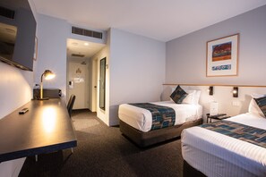 Quarto de hotel com duas camas, uma escrivaninha, uma cadeira e um quadro na parede.