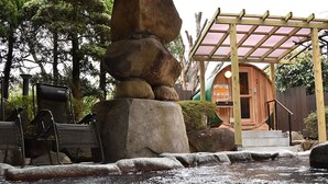 Uma onsen japonesa tradicional com estrutura de madeira, assentos de pedra e um pequeno elemento aquático.