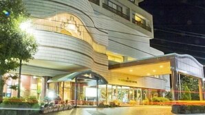 Um hotel moderno com arquitetura curva única, entrada coberta e fachada bem iluminada.