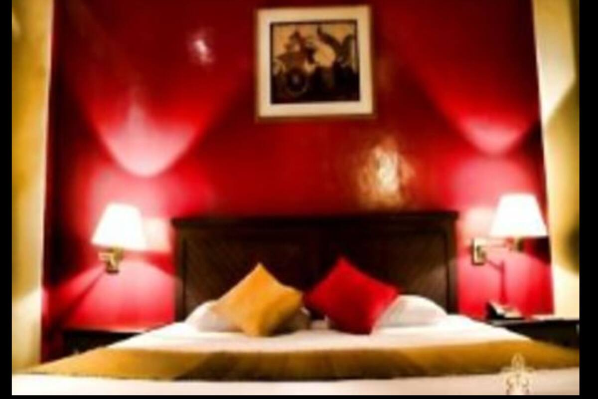 Quarto de hotel com parede vermelha, cama com roupa de cama branca e duas almofadas, e duas luminárias de cabeceira.