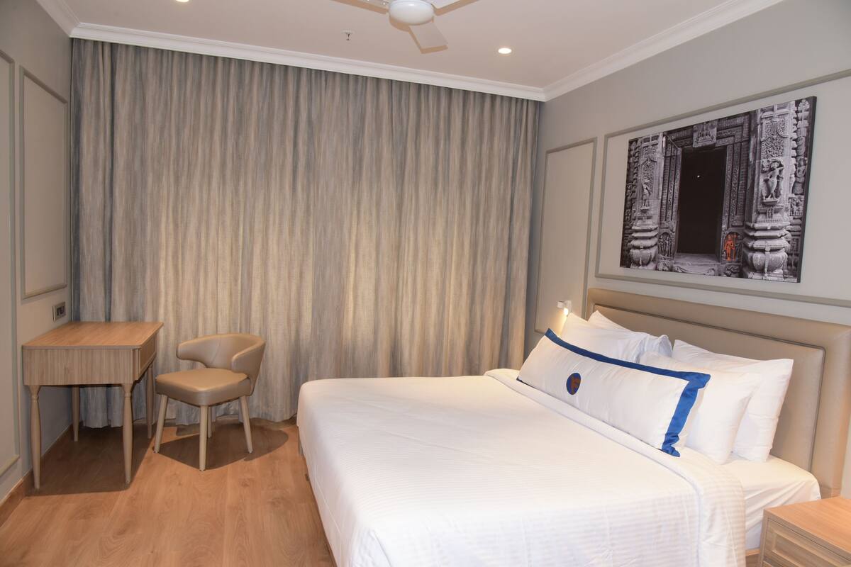 Quarto de hotel com uma cama grande, uma escrivaninha, uma cadeira e um ventilador de teto.