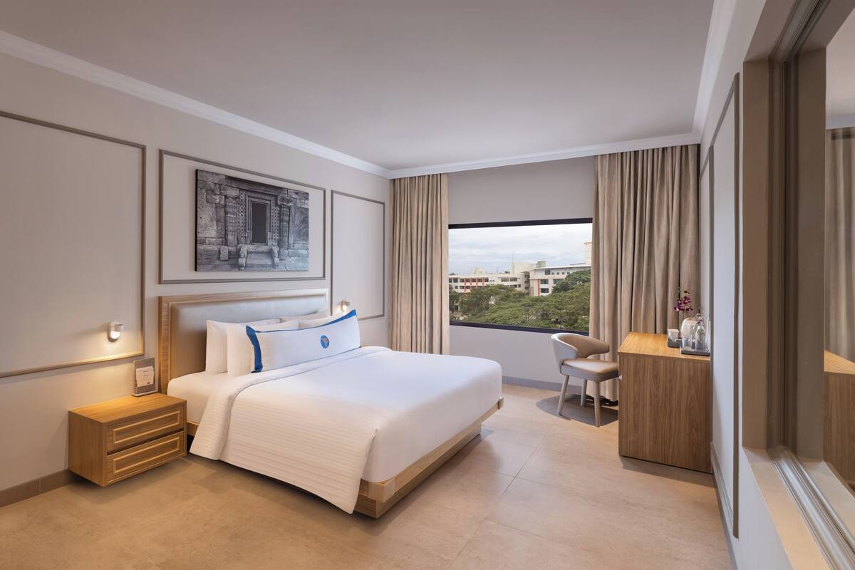 Quarto de hotel moderno com uma cama grande, uma escrivaninha e vista para a cidade.