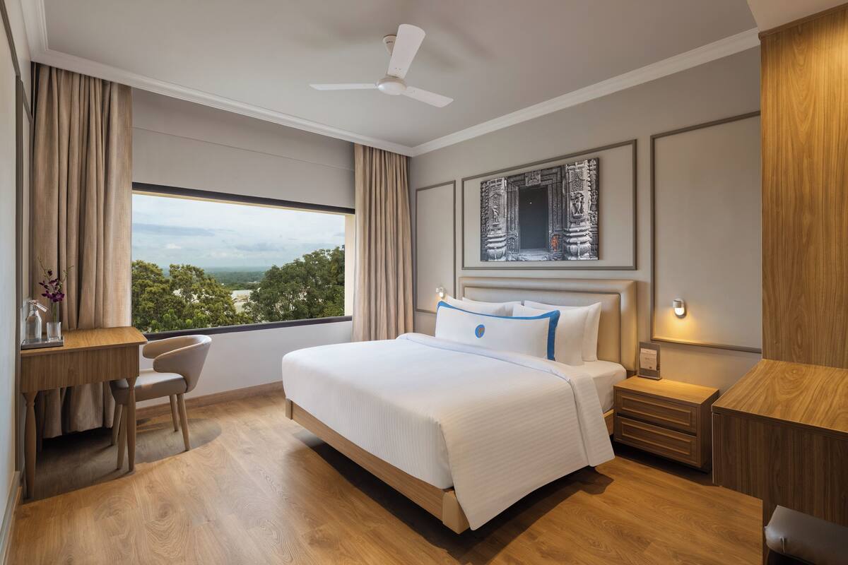 Quarto de hotel moderno com uma cama grande, uma escrivaninha, uma cadeira e vista para o exterior.