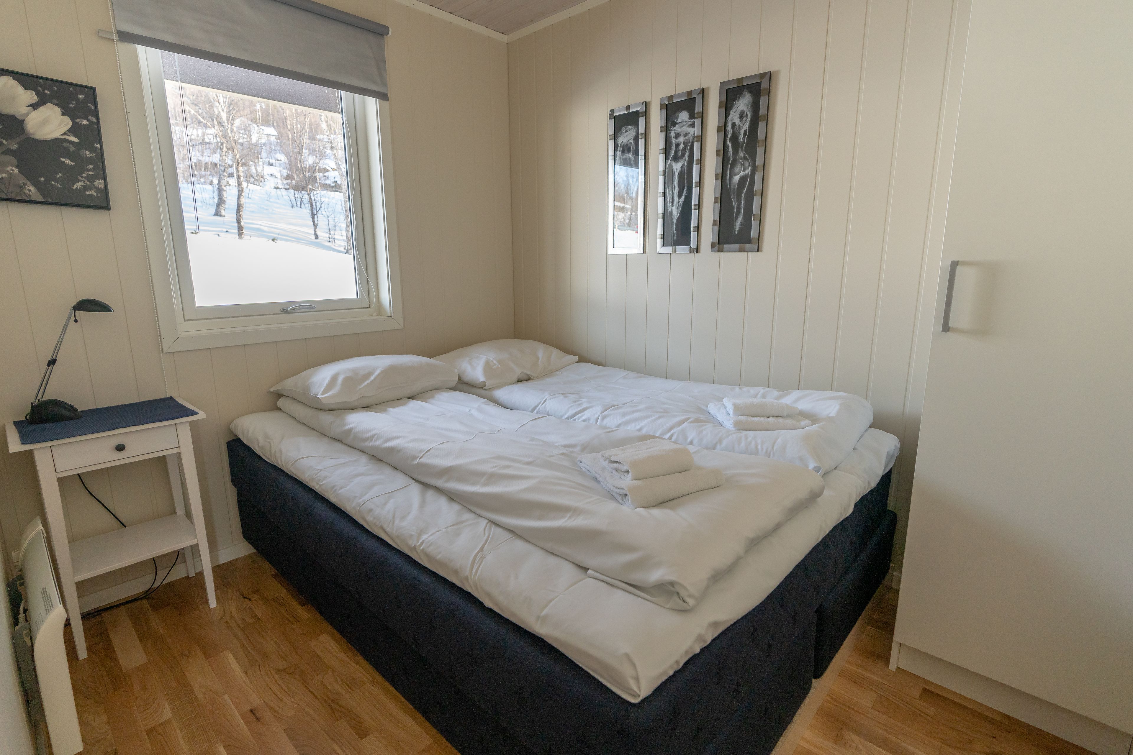 Quarto com cama, escrivaninha e janela com vista para árvores e casas.