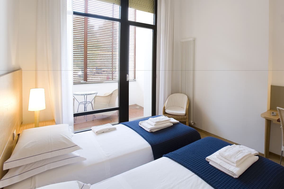 Quarto de hotel com duas camas, uma mesa, uma cadeira e vista para o exterior.
