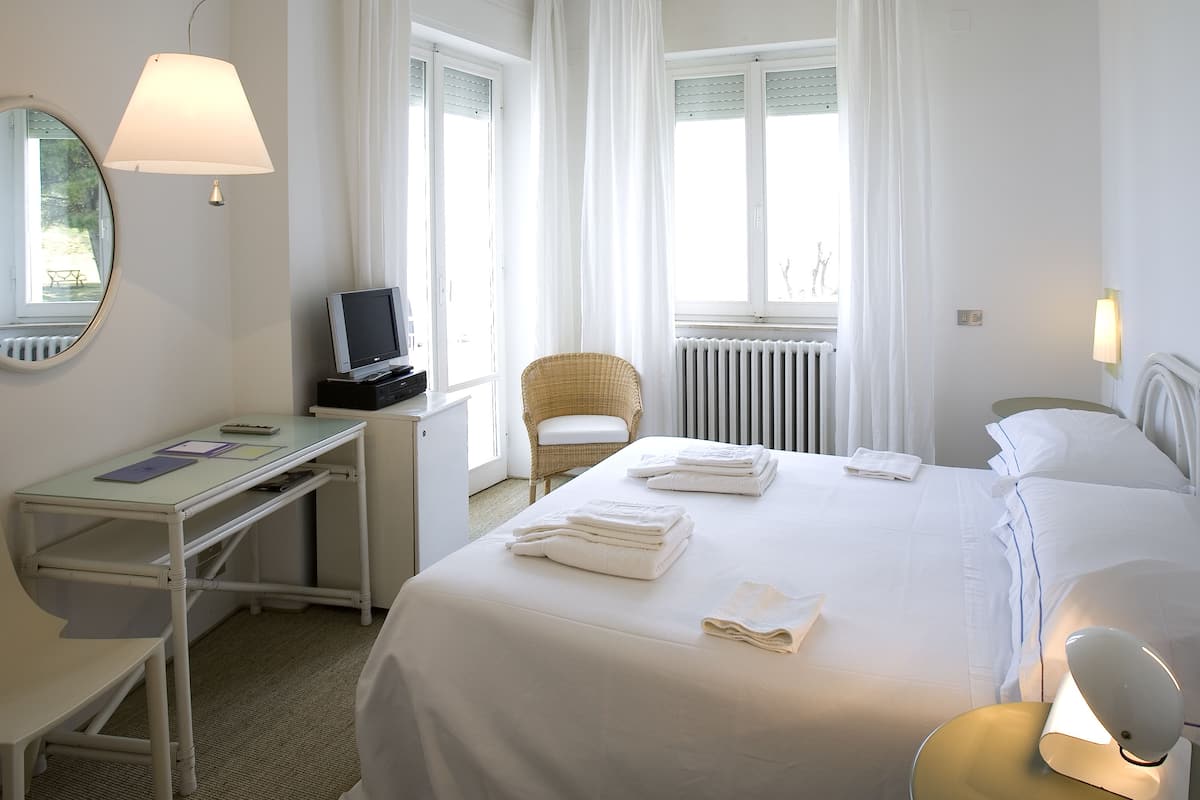 Quarto de hotel com cama, secretária com computador, cadeira e janela com cortinas.