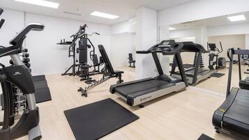 Uma academia com máquinas de cardio, equipamentos de musculação e um espelho.