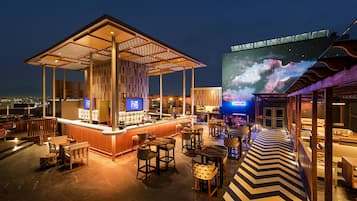 Um bar no terraço com balcão, área de estar e uma grande tela digital exibindo uma cena cósmica.