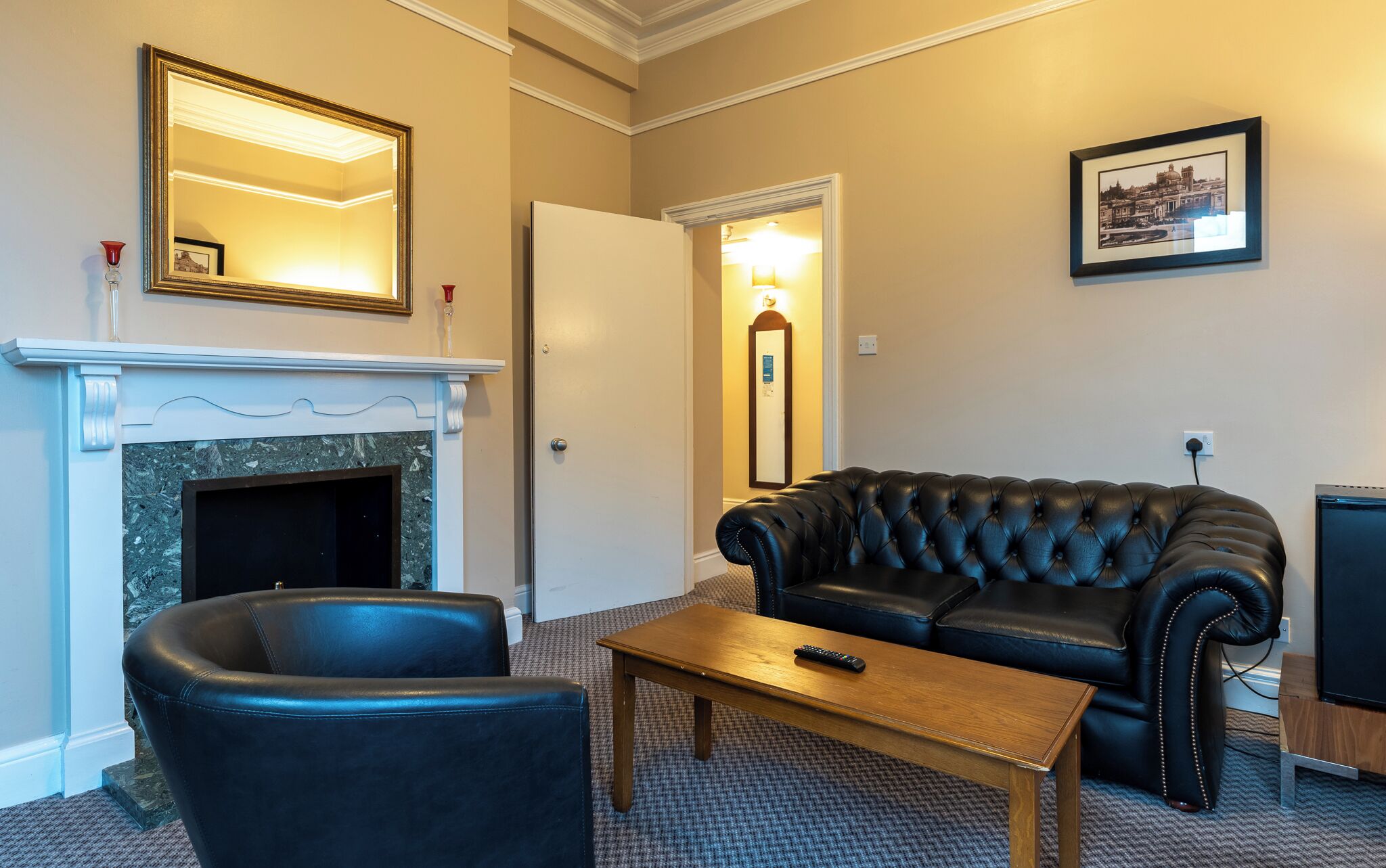 Uma sala de estar com lareira, um sofá de couro preto, uma mesa de centro de madeira e um quadro na parede.