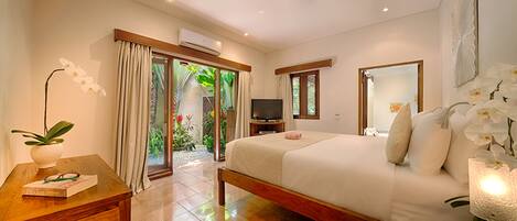 Quarto com cama, televisão, escrivaninha com planta e janela com cortinas.