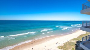 Vista da praia a partir de uma varanda, com céu azul e oceano.