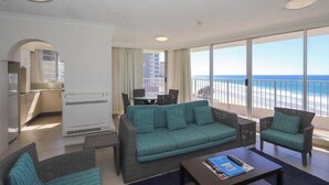 Quarto de hotel com varanda, um sofá, uma cadeira, uma mesa de centro e área de jantar com mesa e cadeiras.