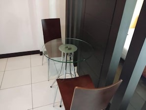 Uma mesa com tampo de vidro e pés de metal, uma cadeira marrom e uma parede de cor escura.