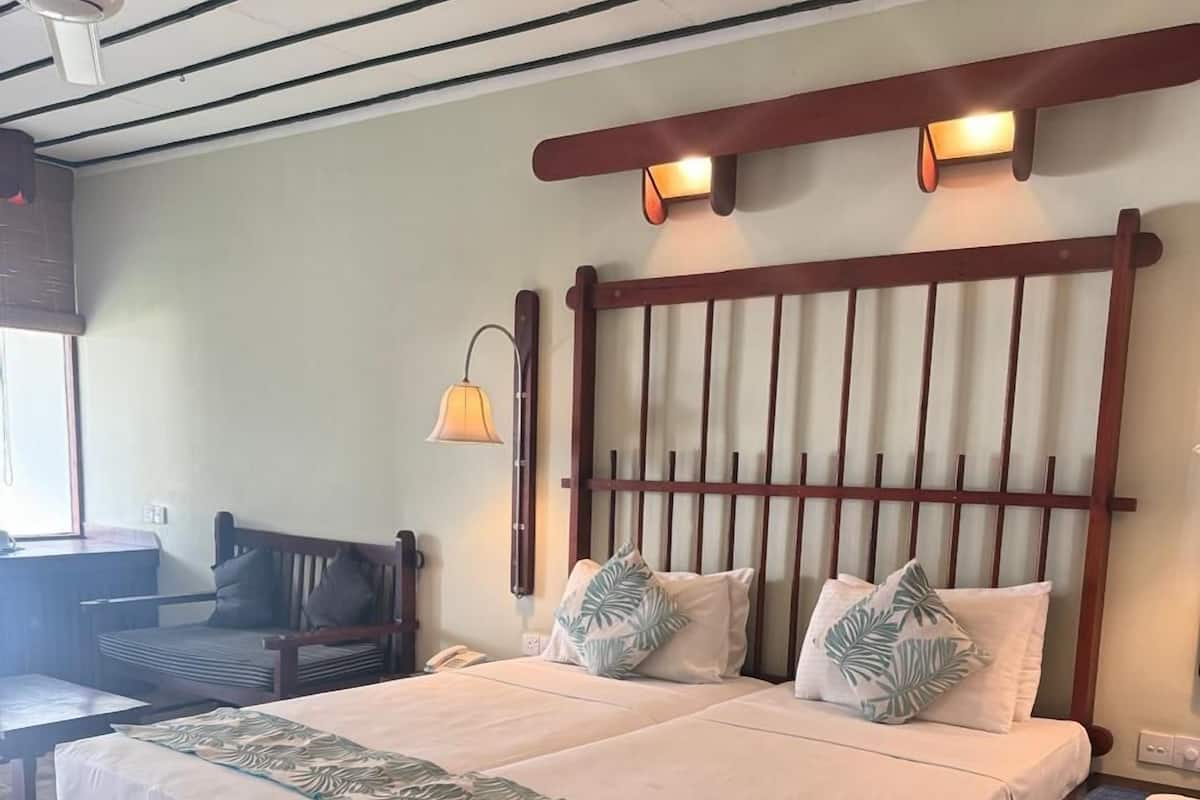 Uma cama de casal com cabeceira de madeira, duas luminárias de cabeceira e uma mesa de cabeceira com um telefone.