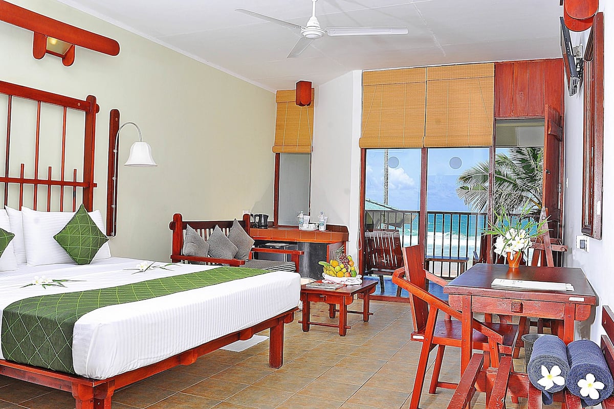 Quarto de hotel com cama, escrivaninha, cadeira, mesa e varanda com vista para o mar.