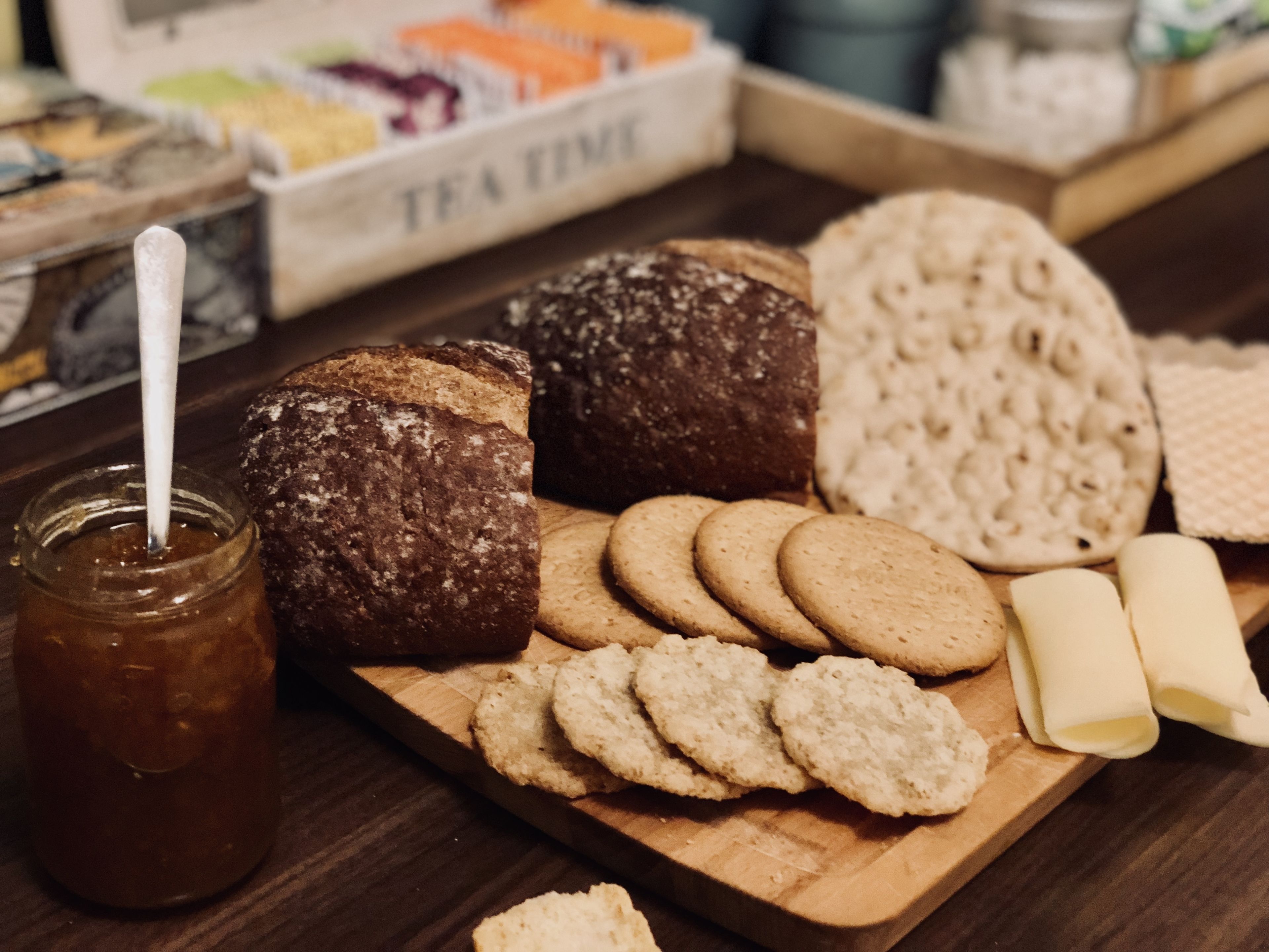 Diversos produtos de panificação em uma tábua de madeira, incluindo pães, biscoitos e torradas.