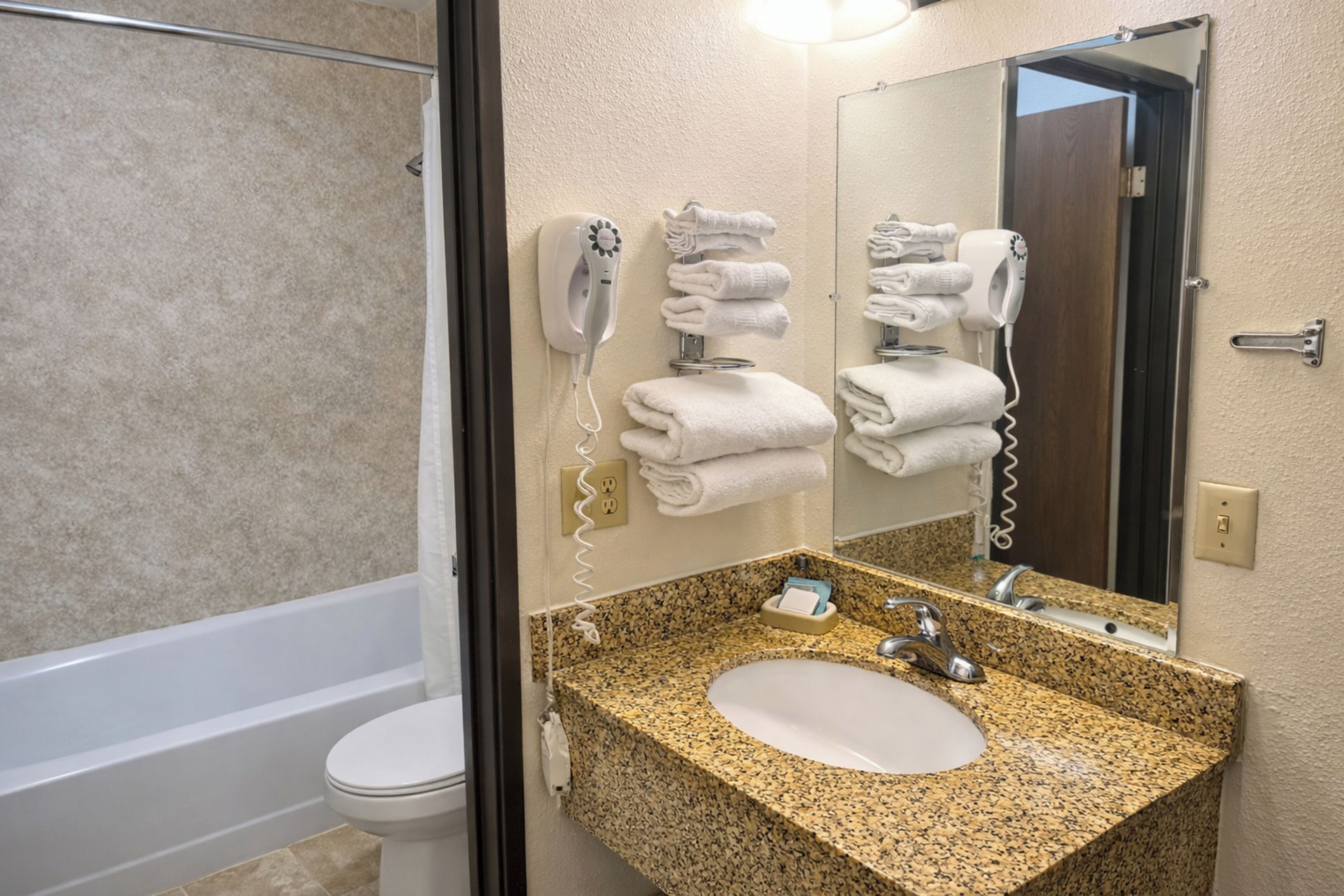 Uma casa de banho com lavatório de granito, um espelho, um porta-toalhas e um secador de cabelo.