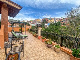 Um terraço com mobiliário de exterior, plantas em vasos e vista para edifícios coloridos ao fundo.