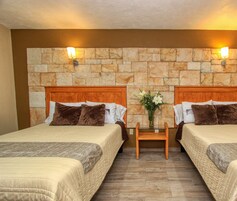 Quarto de hotel com duas camas, uma parede de pedra e uma mesa de cabeceira de madeira com um vaso de flores.