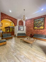 Um hall espaçoso com teto alto, um lustre e um grande mural na parede. Há várias áreas de estar com sofás e uma mesa de centro.