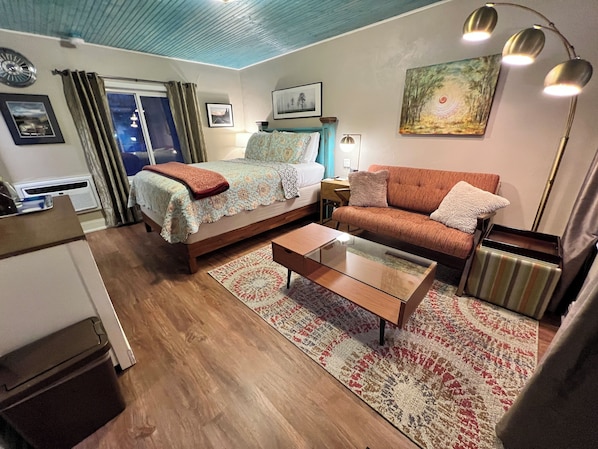 Quarto de hotel com cama, sofá, mesa de centro e um quadro na parede.