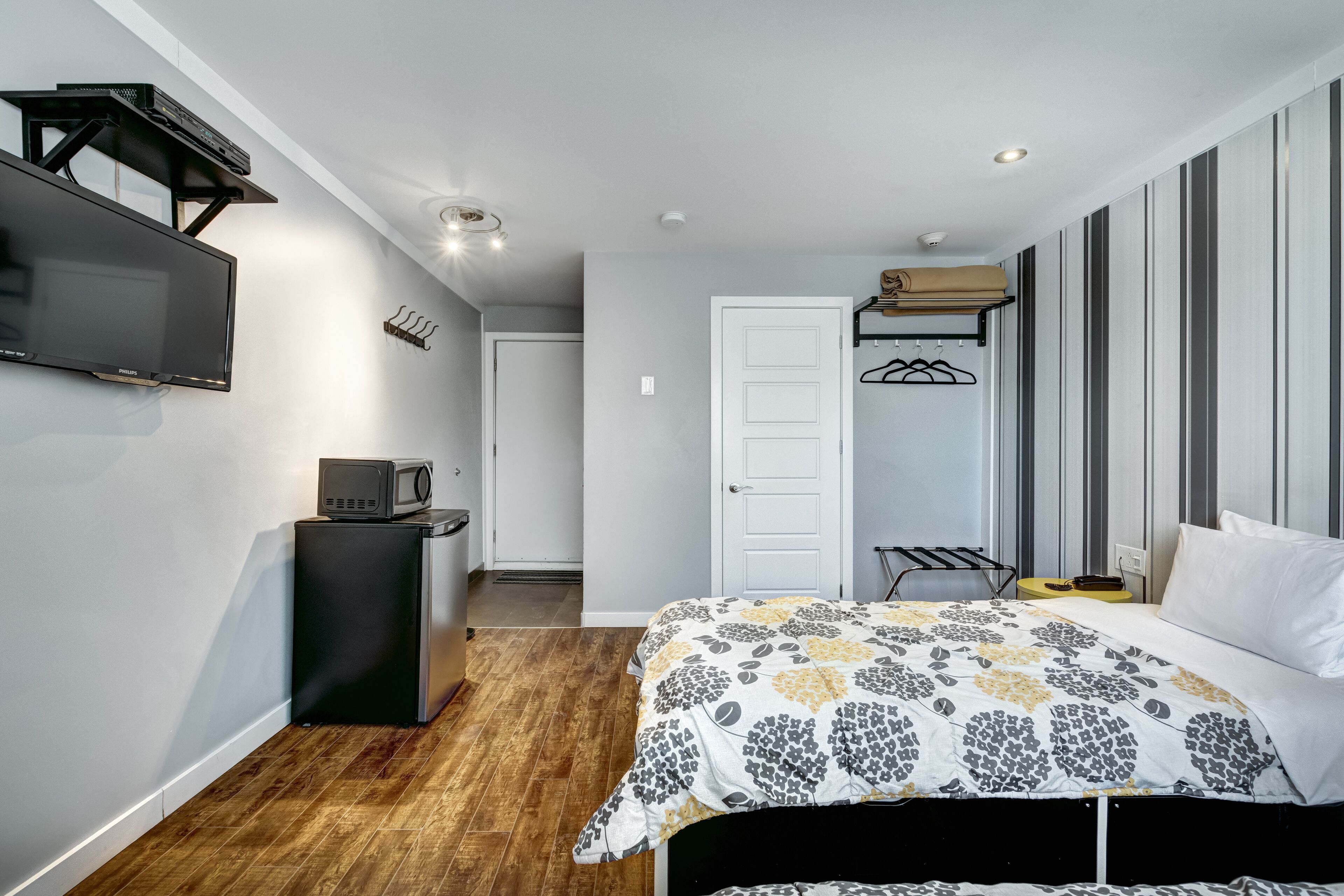 Quarto de hotel compacto com uma cama, uma TV, uma pequena escrivaninha e um guarda-roupa.