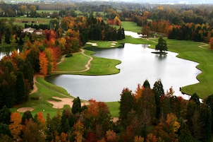Um campo de golfe com um lago, rodeado por árvores de tons outonais.