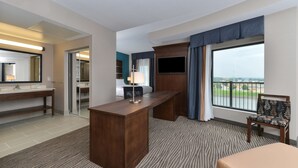 Quarto de hotel com escrivaninha de madeira, cama, televisão e uma janela grande com vista.