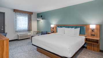 Quarto de hotel com uma cama grande, mesas de cabeceira, escrivaninha, cadeira, janela com cortinas e unidade de ar condicionado na parede.