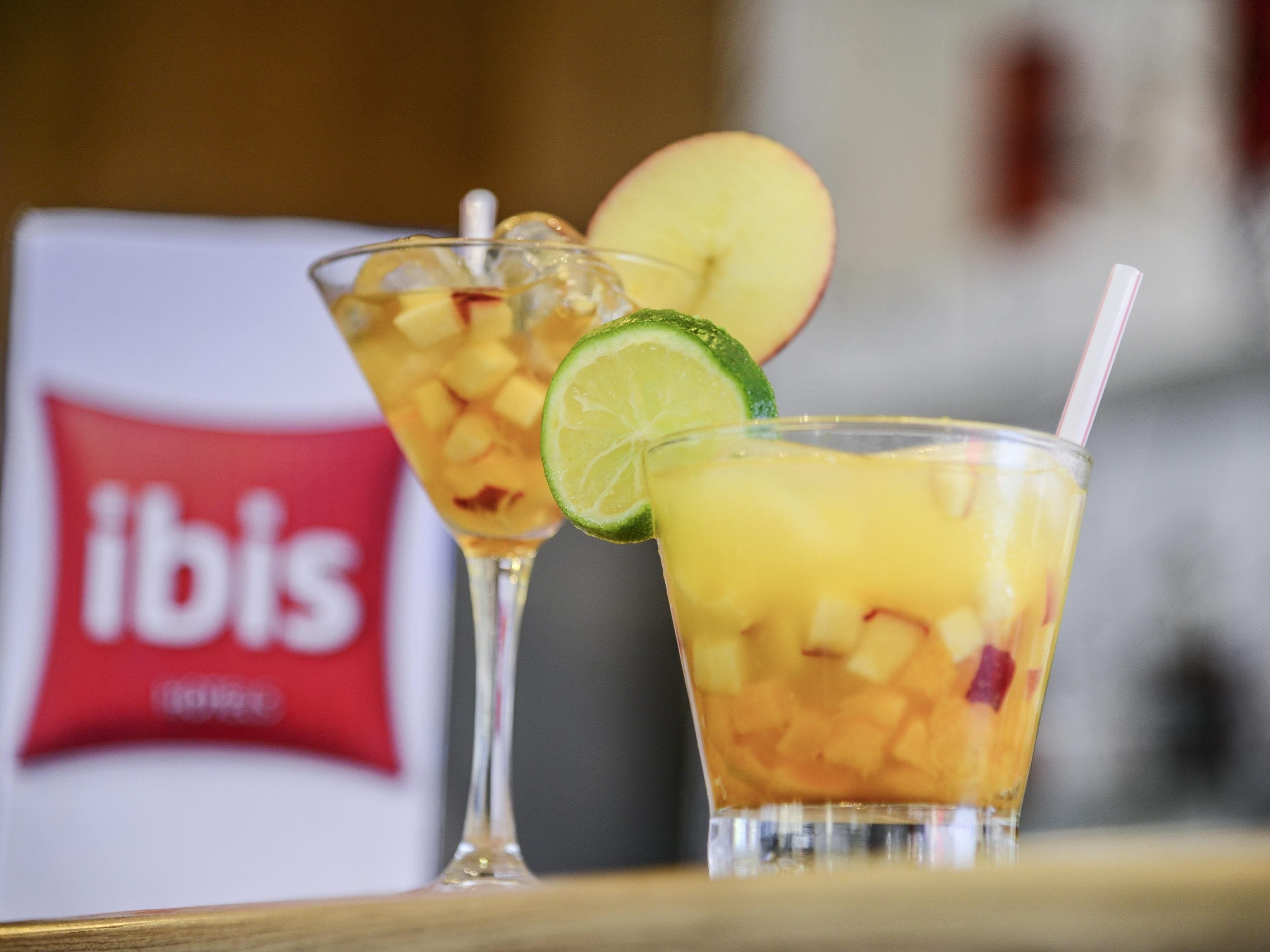 Dois cocktails com fruta e um toque de limão, um copo com canudo, e um fundo desfocado com um letreiro vermelho e branco.