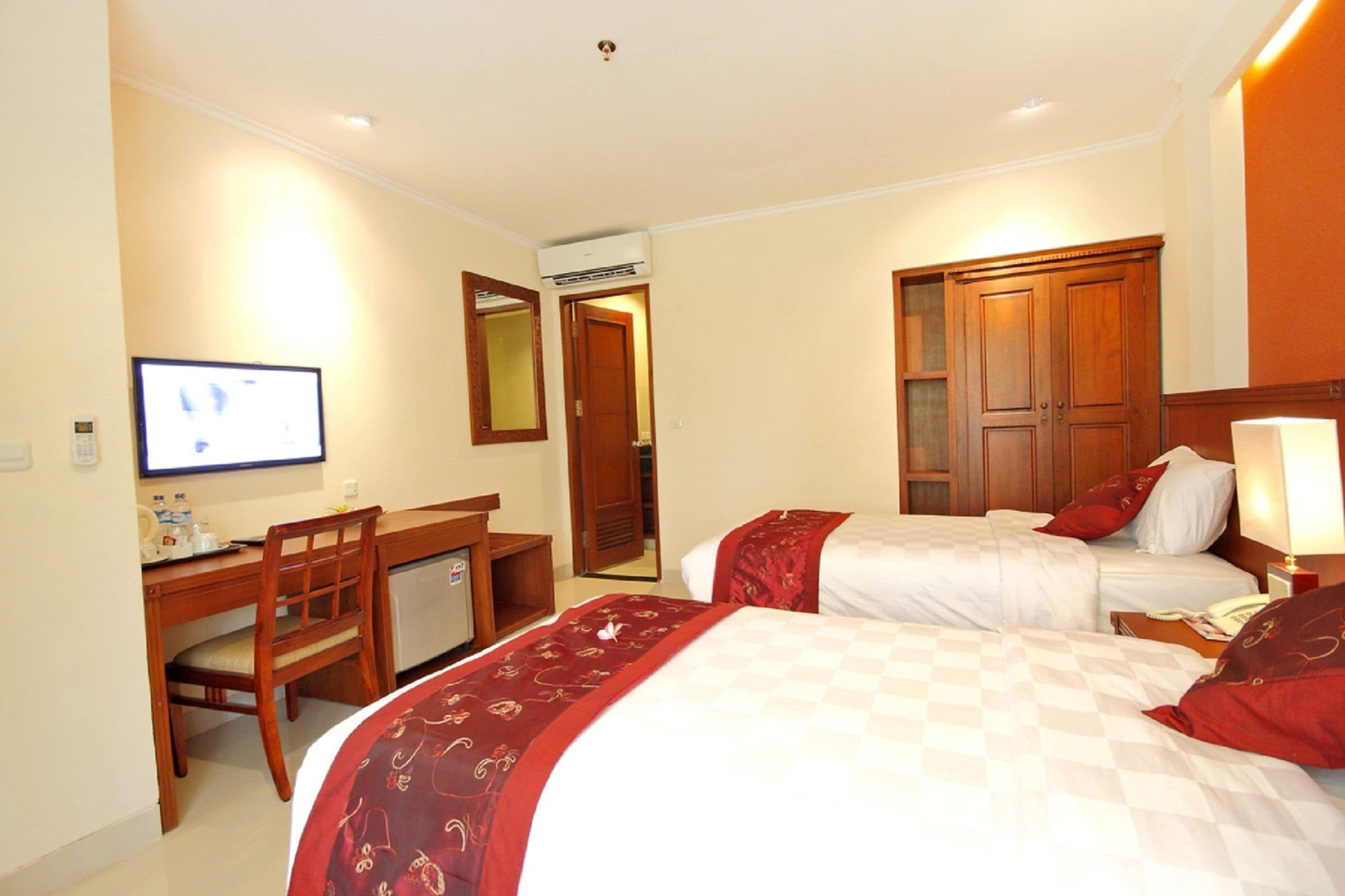 Quarto de hotel com duas camas, uma escrivaninha com cadeira, televisão e um guarda-roupa.