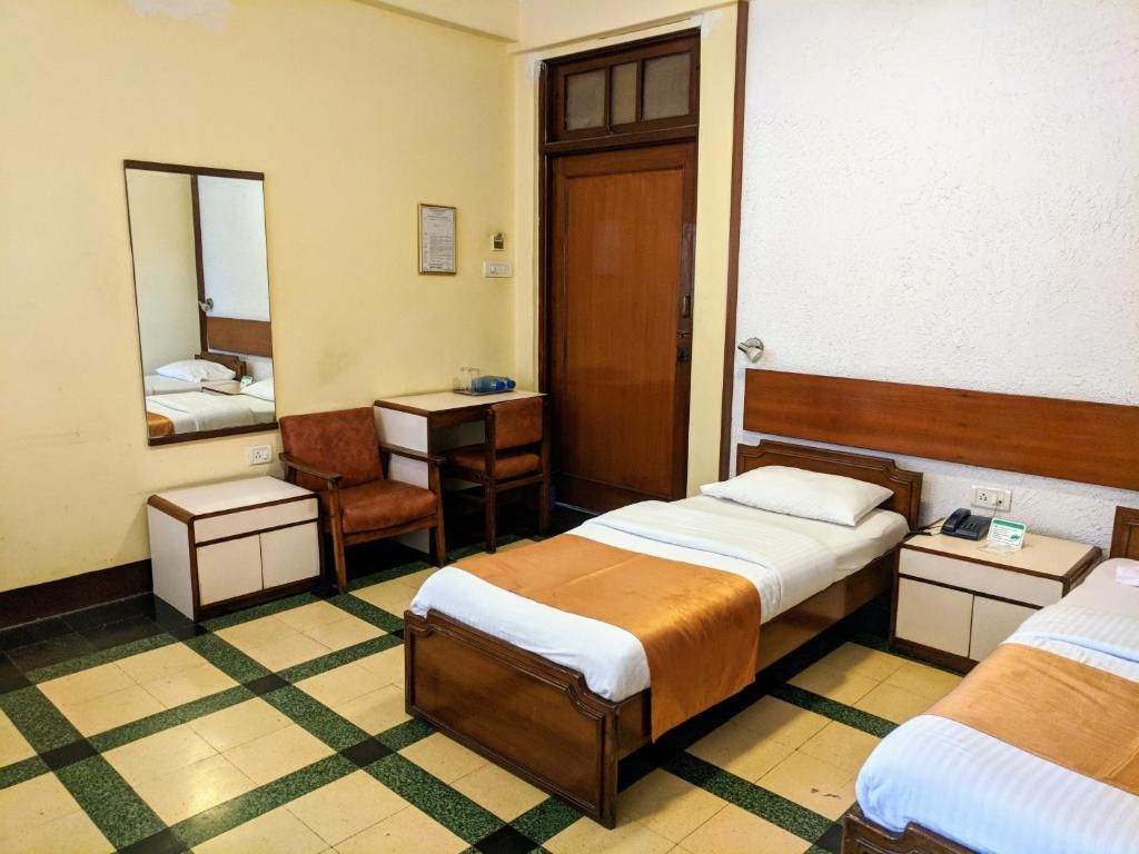 Quarto de hotel com uma cama de solteiro, uma escrivaninha, uma cadeira, uma mesa de cabeceira e um espelho.