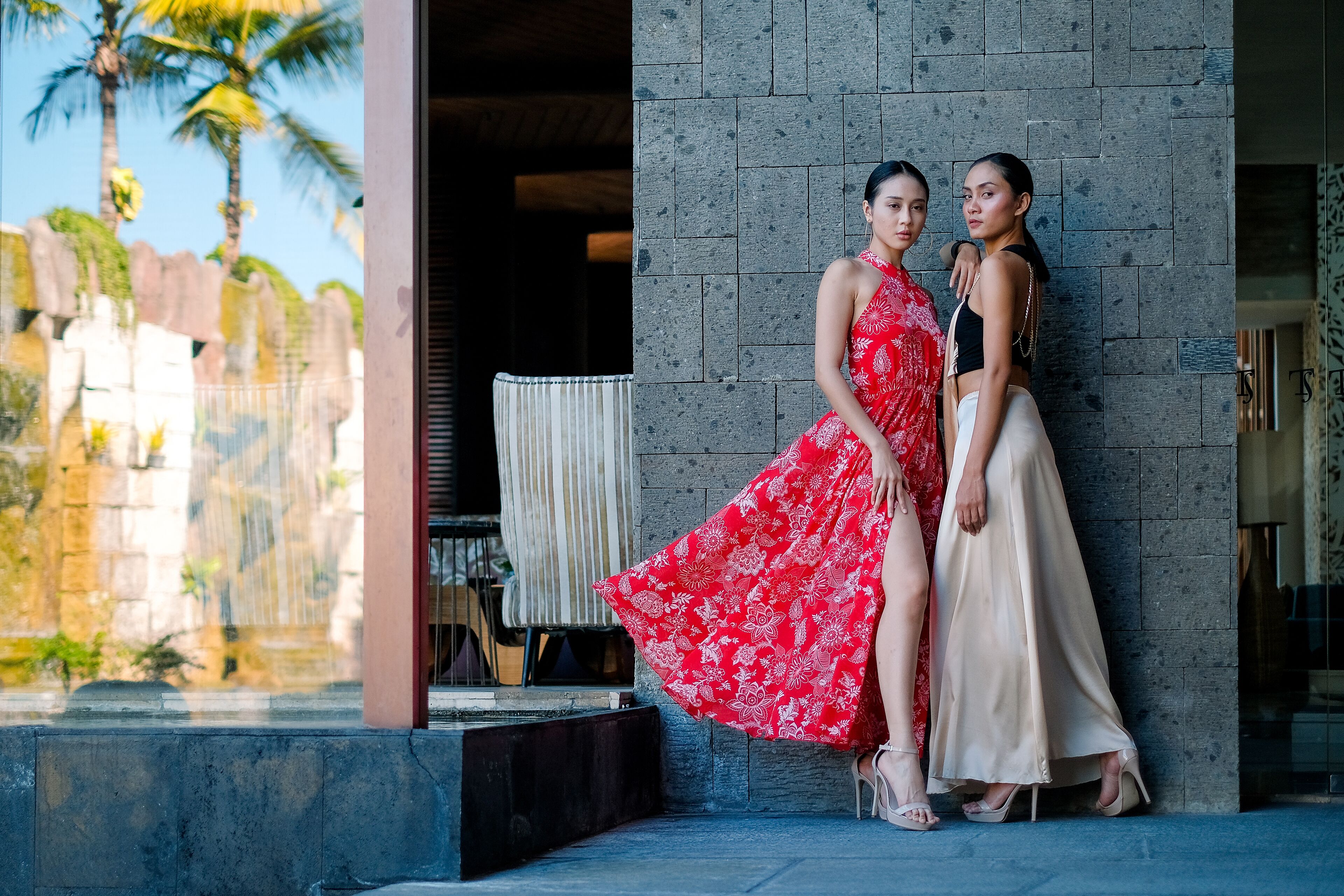 Duas mulheres com um vestido vermelho e bege em frente a um muro de pedra.