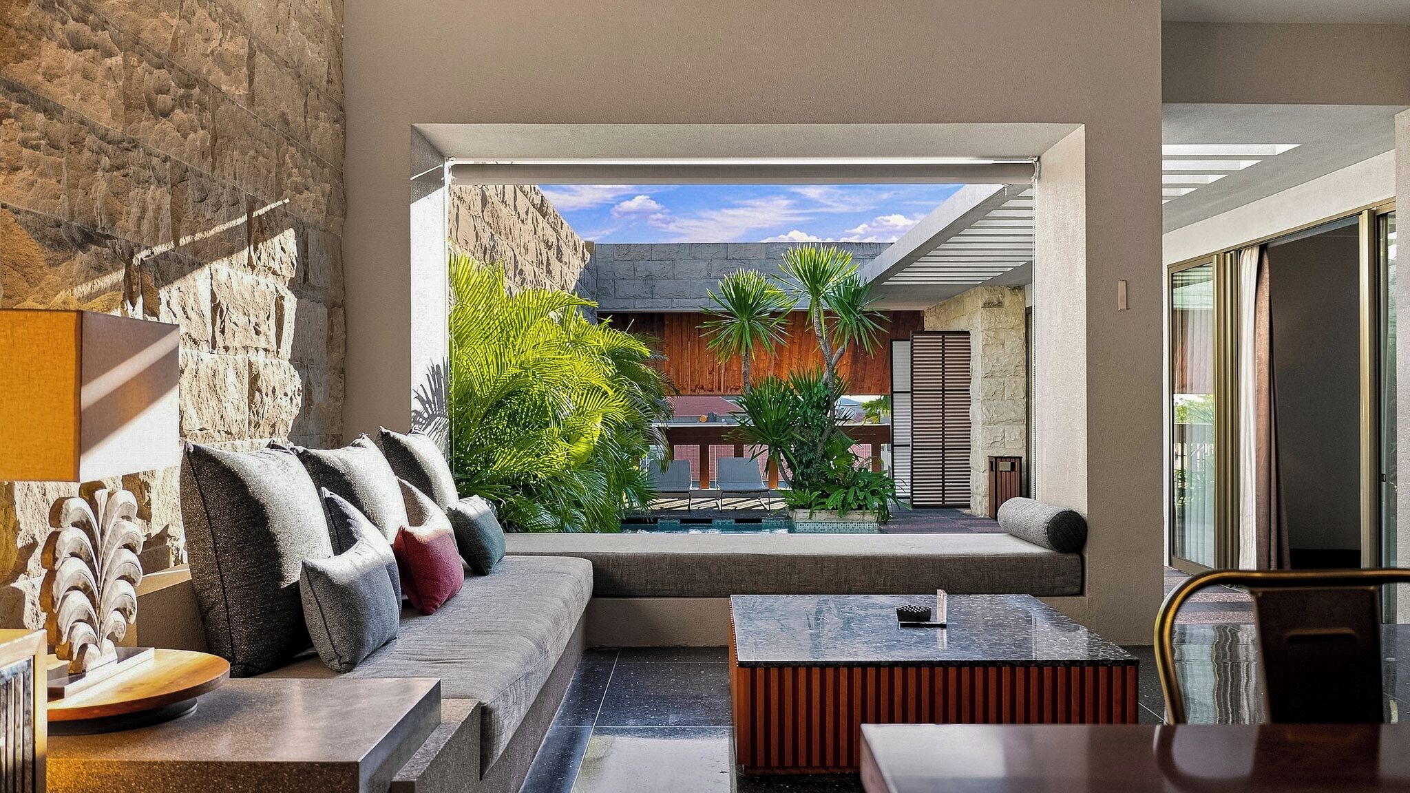 Um interior moderno com parede de pedra, área de estar com almofadas, uma pequena piscina e vista para o exterior.