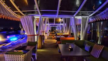 Restaurante interno com mesas, cabines, um deck de madeira e vista para o céu noturno.