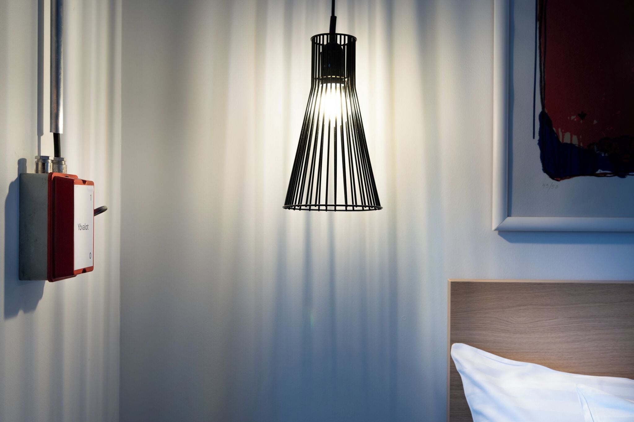 Quarto moderno com luminária pendente, painel de controle e uma obra de arte emoldurada na parede.