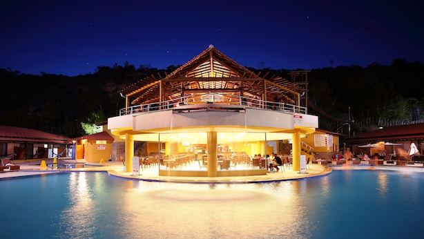 Uma área de piscina com um espaço de estar coberto e um edifício com vários andares.
