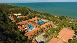 Vista aérea de um resort com piscina, palmeiras e praia.