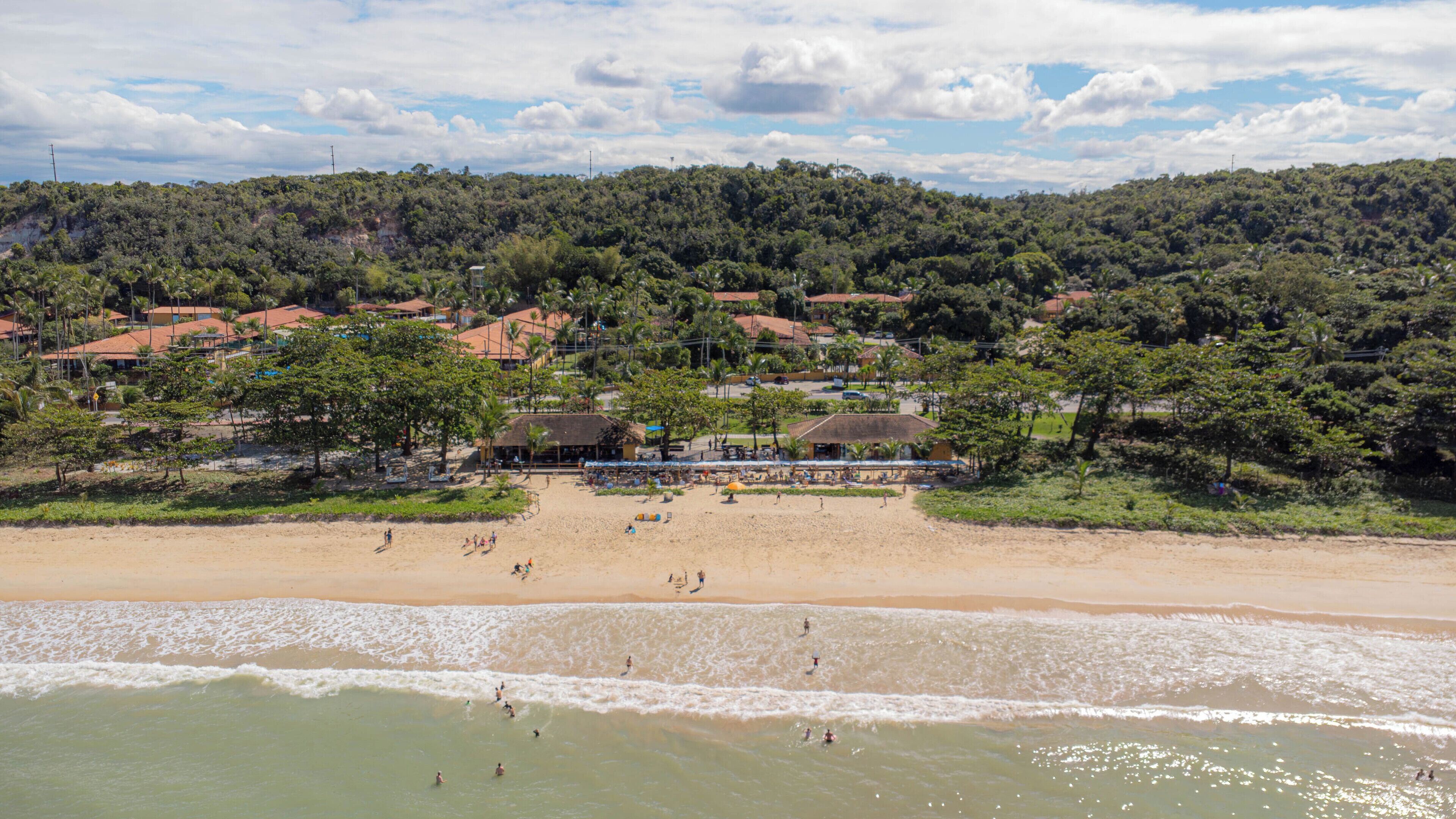 Uma praia com pessoas nadando e tomando sol, cercada por casas e árvores.