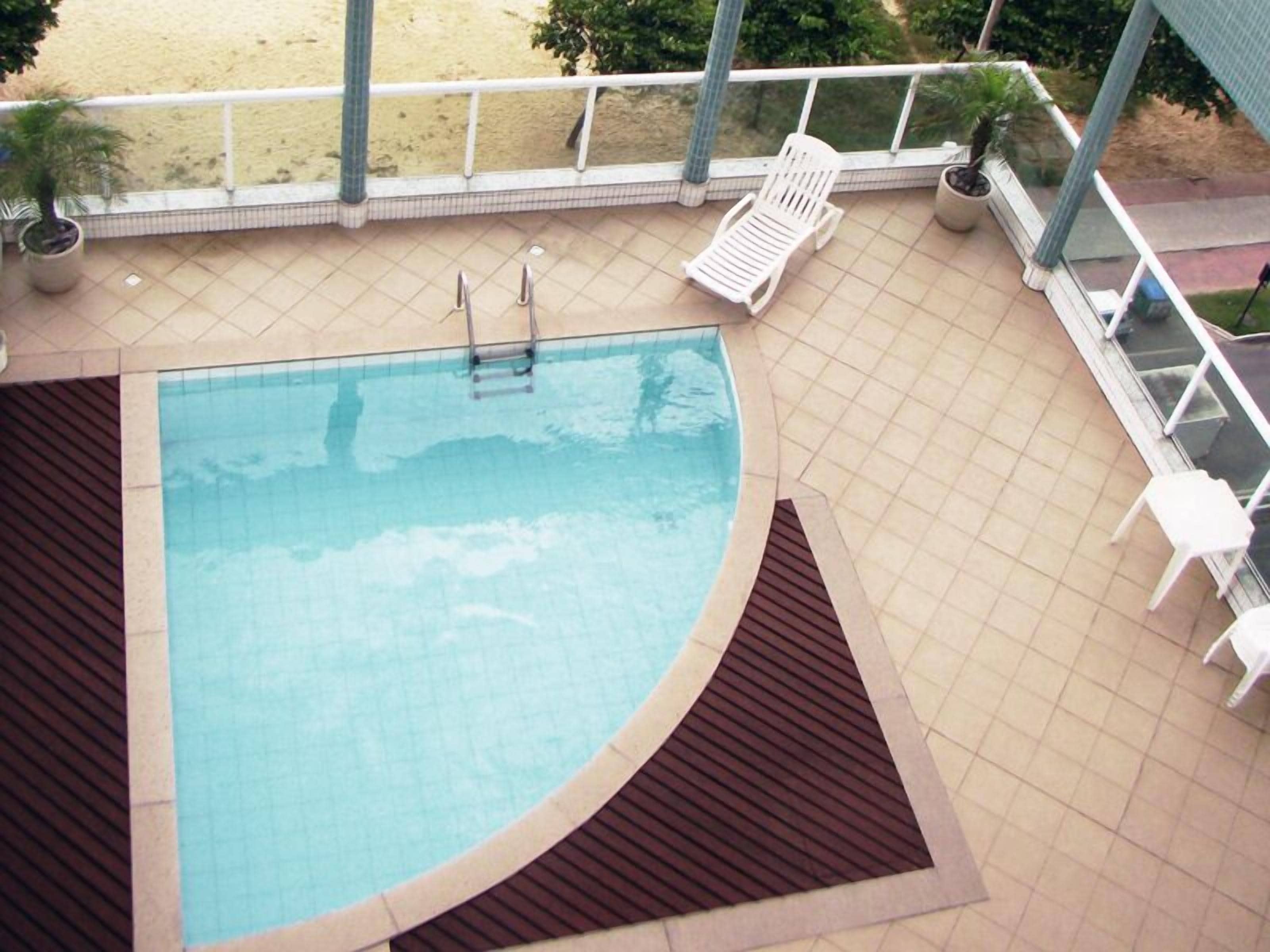 Uma piscina com deck de madeira, cadeiras de descanso brancas e plantas em vasos.