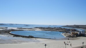 Uma área costeira com uma piscina grande, praia e um edifício com fachada azul.