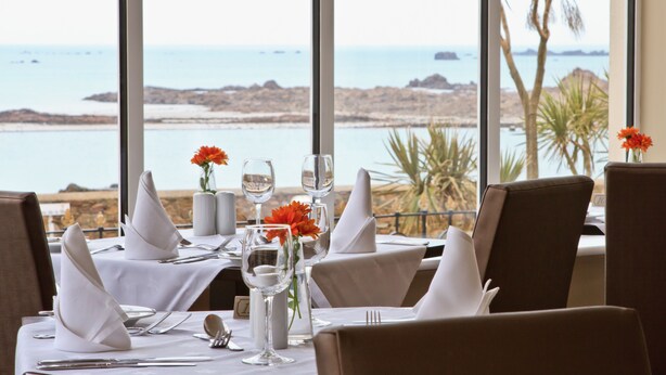 Mesa de jantar posta para dois, com vista para o mar e costa rochosa.