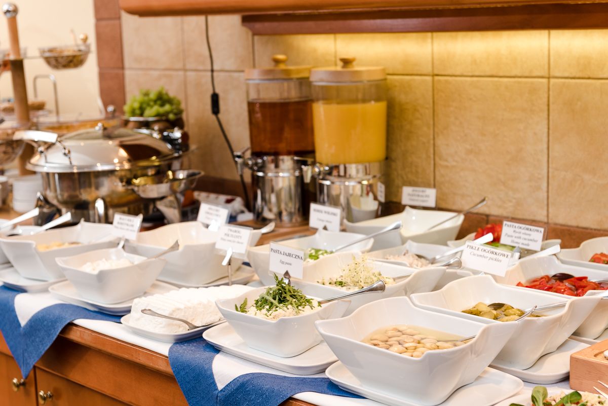 Buffet com diversas opções de comida, incluindo massas, saladas e outros pratos, dispostos sobre uma mesa com um americano azul.